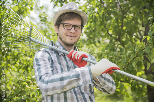 "a young male farmer holding a rake and smiling in the garden ...