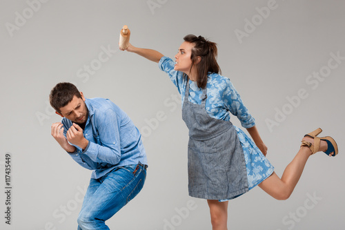 "Young woman beating man with rolling pin over grey background." Stock ...