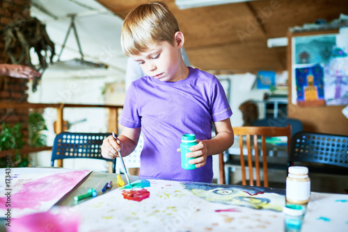 "Portrait of blonde little boy painting pictures carefully, standing at ...