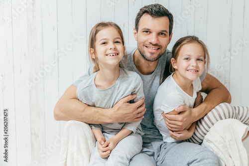Portrait Of Happy Young Father Embraces His Two Daughters Loves Them
