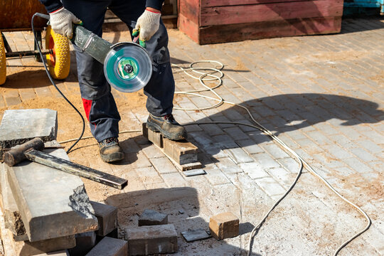 The Worker Cuts A Metal Plate And Paving Slabs For Laying On The ...
